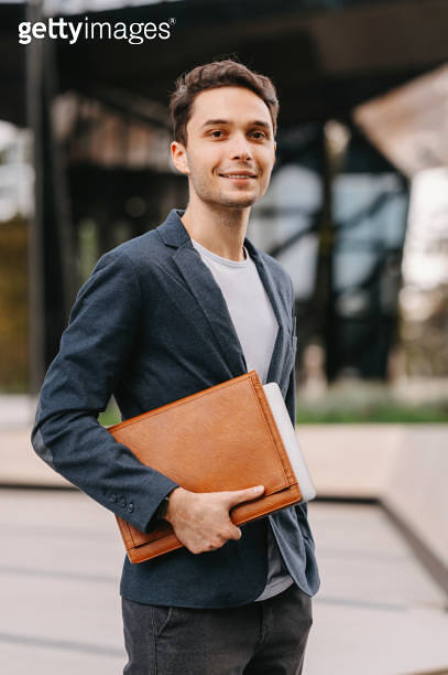 Young man holding important papers stands outdoors near a business ...