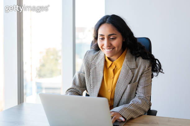 Latina businesswoman smiling and working with laptop in her office ...