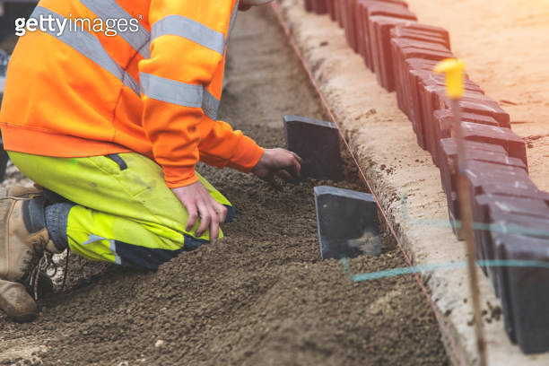 Groundworker in hi-viz leveling semi-dry concrete and kerbs on new road ...