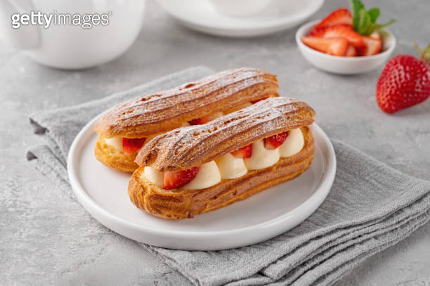 Eclairs with cream and fresh strawberries sprinkled with powdered sugar on top on a gray ...