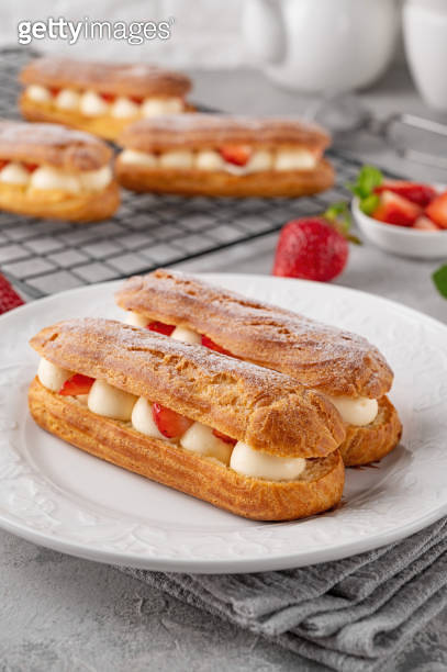 Eclairs with cream and fresh strawberries sprinkled with powdered sugar on top on a gray ...