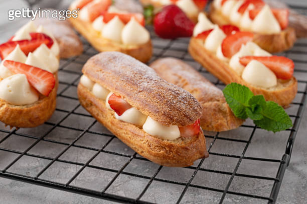 Eclairs with cream and fresh strawberries sprinkled with powdered sugar on top on a gray ...