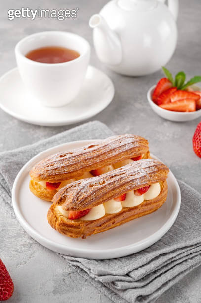 Eclairs with cream and fresh strawberries sprinkled with powdered sugar on top on a gray ...