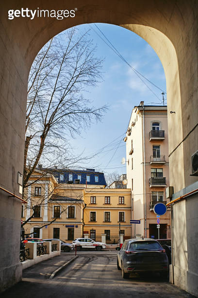 Passage arch in a house onto a street with parked cars and buildings ...