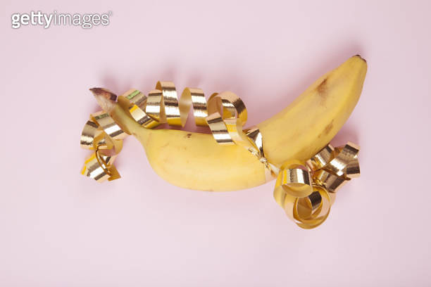 a ripe banana wrapped in a golden curled ribbon as if it were a gift ...