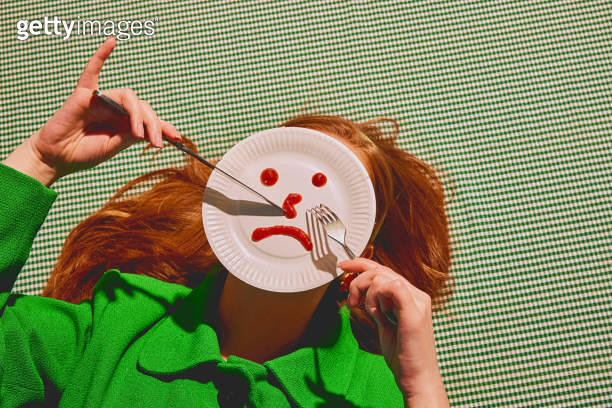 Young redhead woman lying with knife and fork over paper plates showing ...