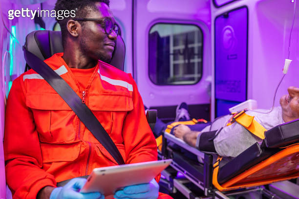 Paramedic using digital tablet while transporting patient in ambulance ...