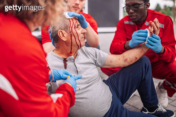 Paramedics providing first aid to injured man bleeding from head wound ...
