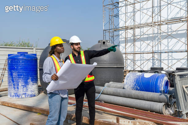 Two construction worker standing together in front of a large building ...