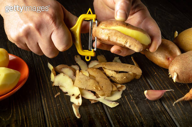Man hands peel raw potatoes with a potato peeler in the kitchen at home ...