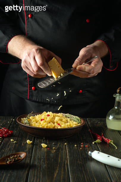 A cook grates hard cheese into a plate of pasta with a hand grater ...