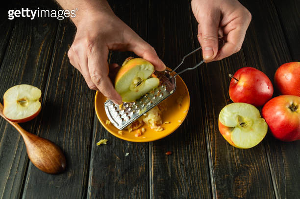 Using a hand grater to grate apples. Close-up of a chef hands preparing ...