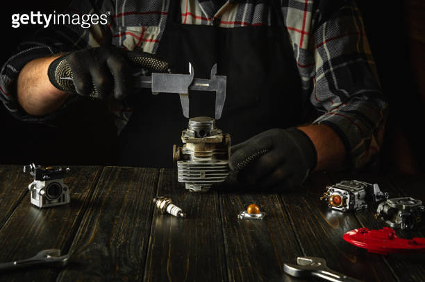 A foreman at a workbench in a workshop repairs a chainsaw engine after ...