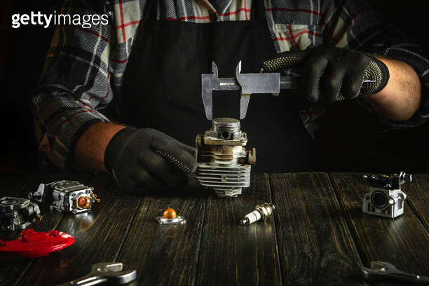 A foreman at a workbench in a workshop repairs a chainsaw engine after ...