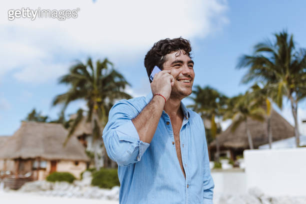 hispanic young man talking by mobile phone at the beach on vacations or ...