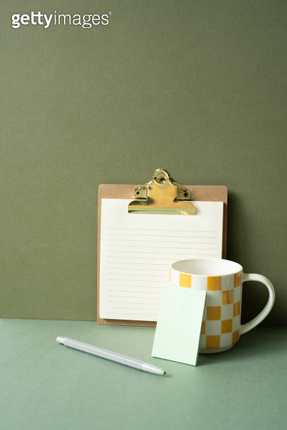 Workspace notepad binder clip, pen, mug cup on green desk. khaki wall ...