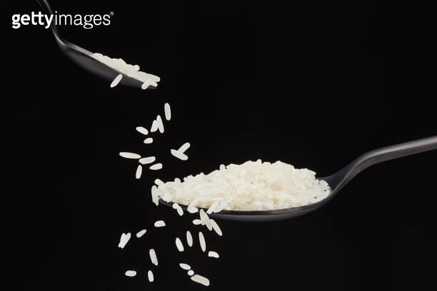 Falling rice grains from a small spoon into a big spoon on a black ...