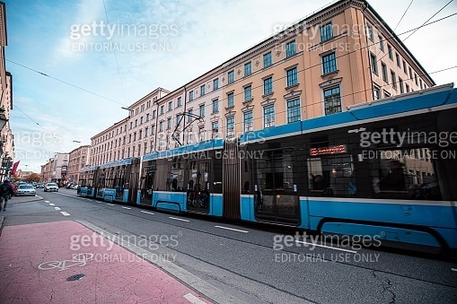 A blue streetcar travels along a city street in Munich, Germany ...