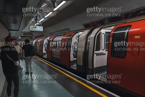 A red train in a London underground station with people waiting on the ...