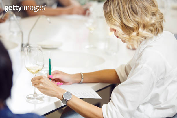 Young handsome looking woman tasting white wine and writing notes to ...