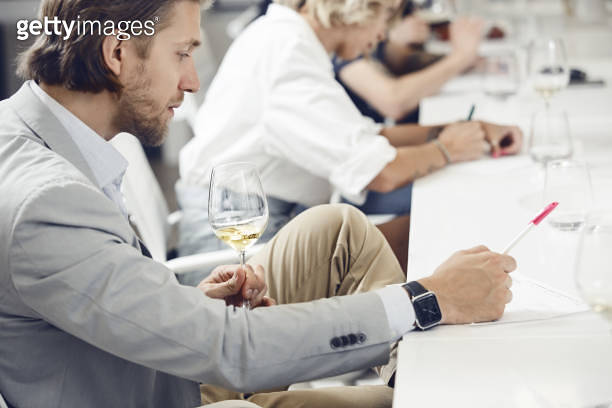 Successful looking male sommelier tasting white wine into glass and ...