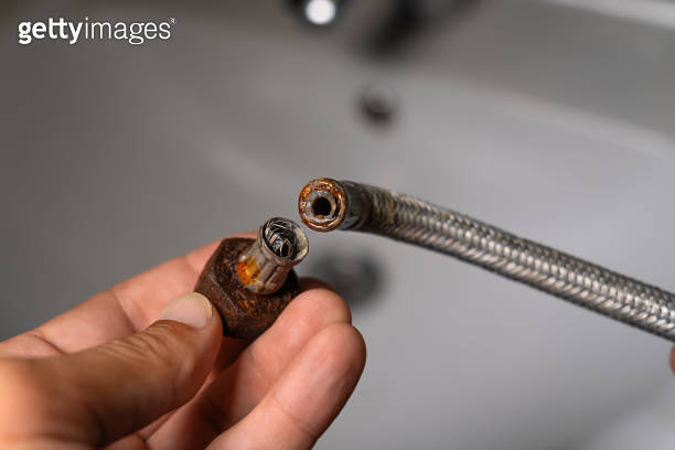 Plumber close-up holds used broken hose all rusty and on neck of ...