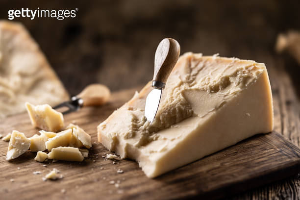 A block and pieces of Parmesan cheese on a cutting board along with a ...