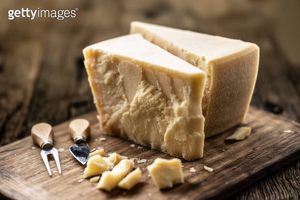 A block and pieces of Parmesan cheese on a cutting board along with a ...