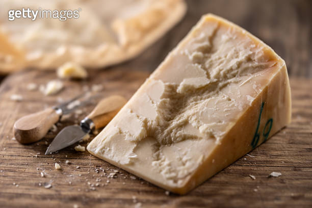 A block and pieces of Parmesan cheese on a cutting board along with a ...