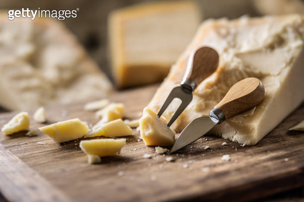 A block and pieces of Parmesan cheese on a cutting board along with a ...