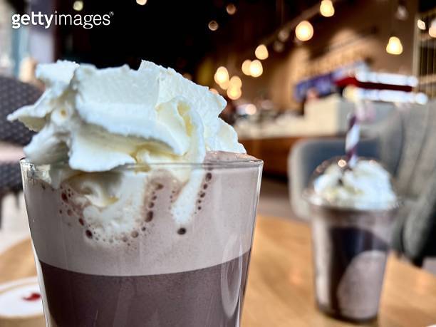 A drinking glass of hot chocolate topped with fresh whipped cream on a ...