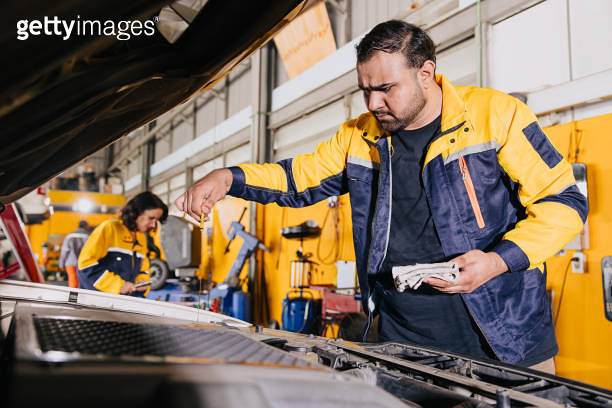 Garage auto mechanic worker working check engine oil level stick in car ...