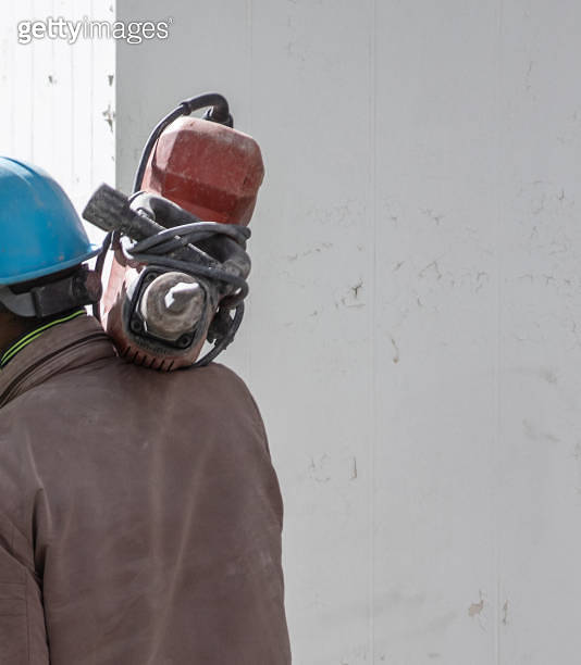 Construction worker leaving site and carrying a concrete breaker on his ...