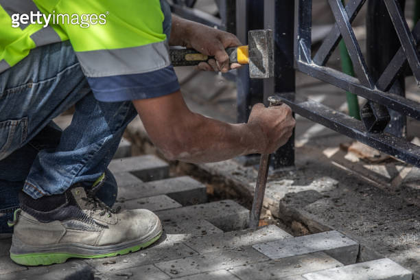 Building construction worker wearing florescent top hammering a chisel ...