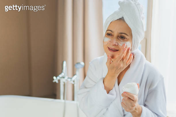 Mature adult old woman applying nourishing anti age face cream doing daily beauty routine Senior ...