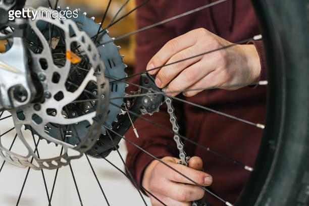 A close-up of the bike mechanic's hands putting the chain on the rear ...