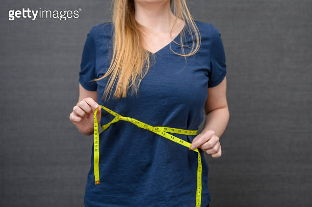 A woman measures her waist circumference with a yellow tape measure 이미지 ...