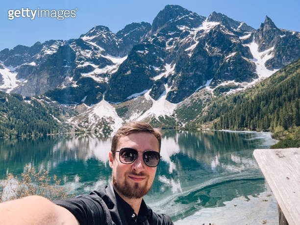 Male portrait selfie in the mountains, lake at the background ...