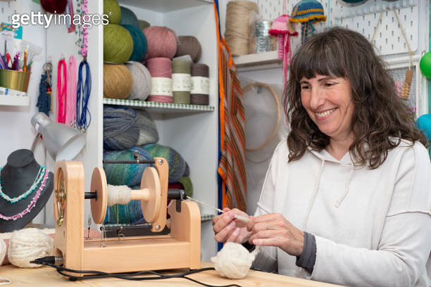 Smiling craftswoman spinning wool with an electric spinning wheel in ...