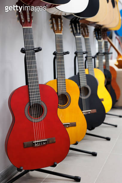Acoustic guitars of different sizes and colors on the stands in the ...