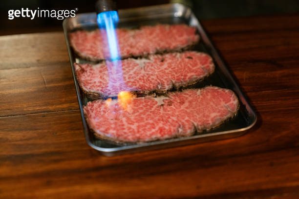 Kitchen torch burn on fresh beef raw sliced with marbled texture on ...