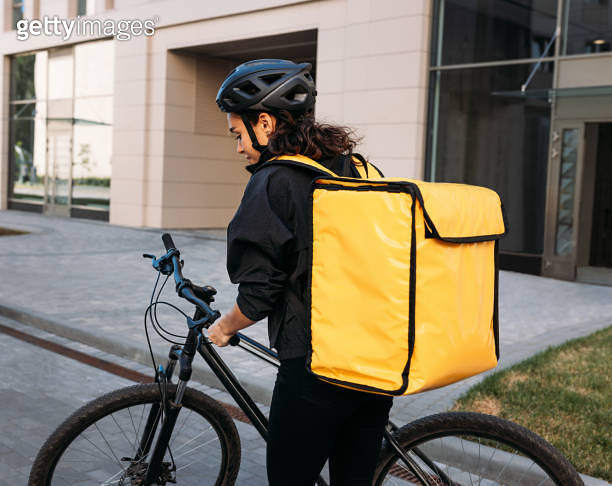 Back view of a female courier standing on a street with a bicycle. Rear ...