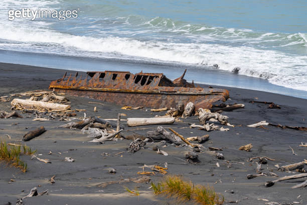 Old wrecked hulk of washed-up boat rusty and surrounded by driftwood in ...