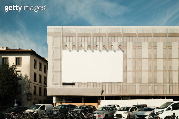 Large blank billboard with spotlights hanging on modern building facade ...