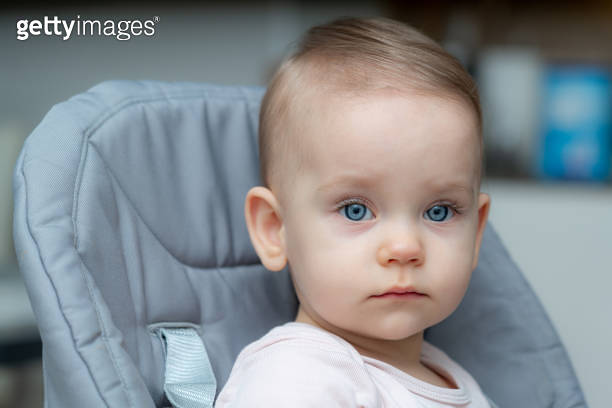 Close-up of a toddler baby gazing at the camera with calm face sitting ...
