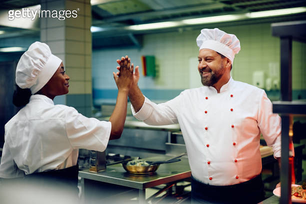 Happy professional chefs giving high-five while working in restaurant ...