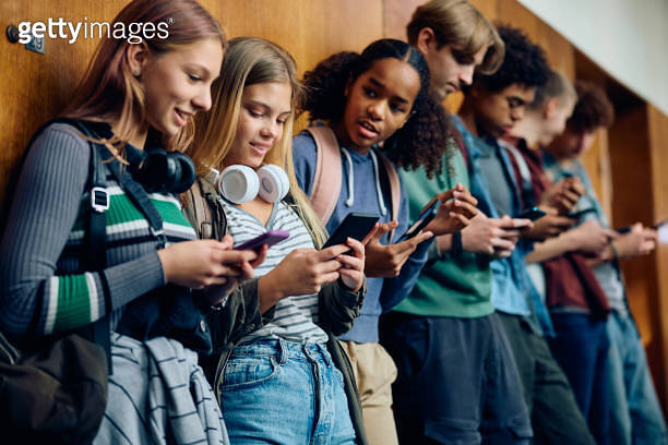 Multiracial group of high school students using their cell phones in ...