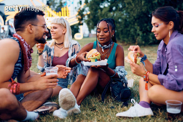 Multiracial group of friends eating hamburgers and drinking beer while ...