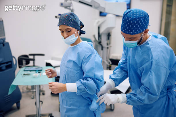 Male nurse tying surgical gown of female doctor before getting into the ...