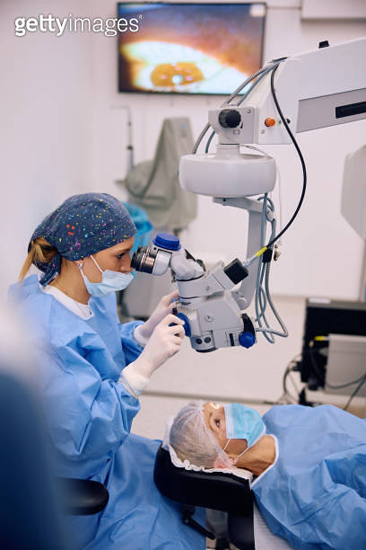 Ophthalmologist looking through microscope during eye surgery of mature ...